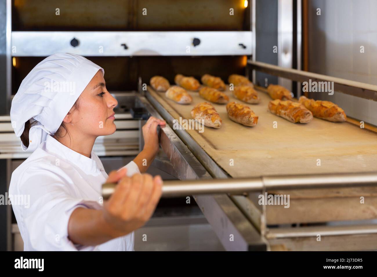 Female bakery worker pulls bread pan out of oven Stock Photo - Alamy