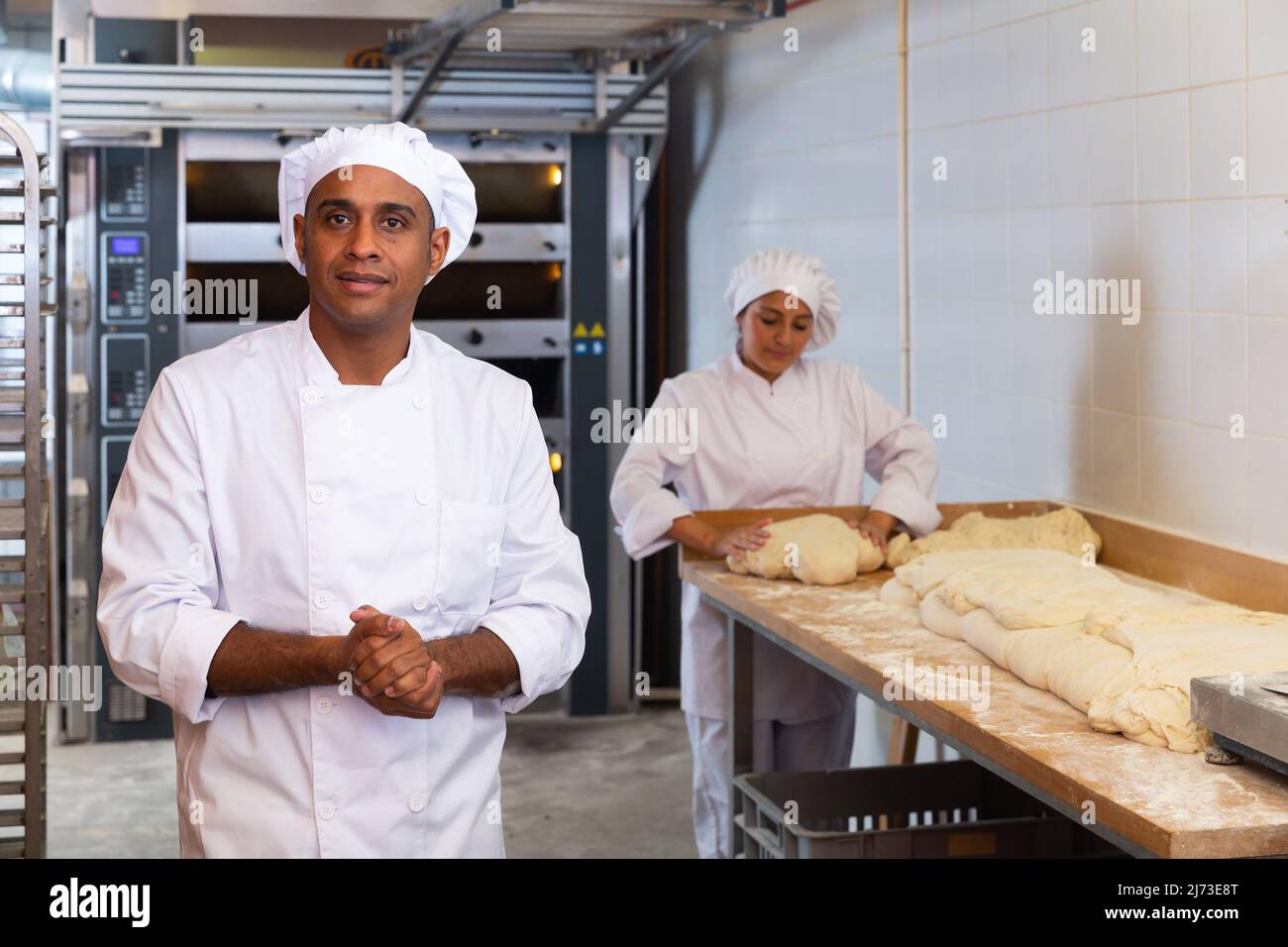 Confident bakery owner posing against busy workers background Stock ...