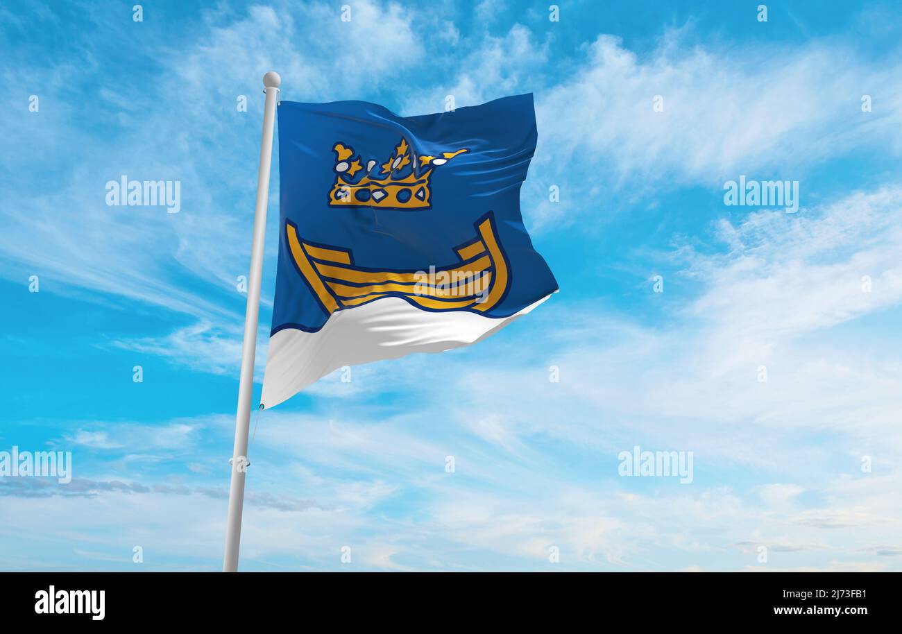official flag of Helsinki , Finland at cloudy sky background on sunset ...