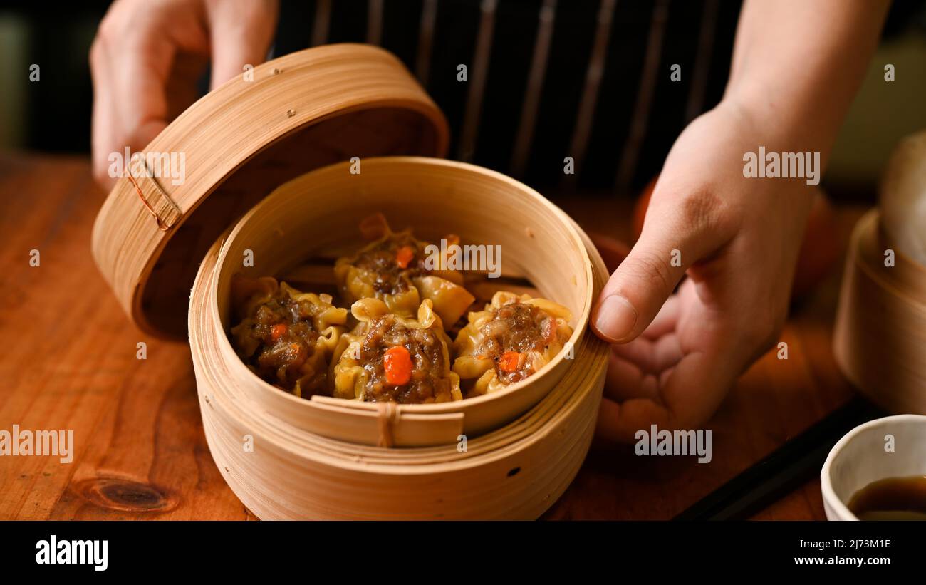 Female chef open a fresh hot bamboo steamer with steamed shrimp ...