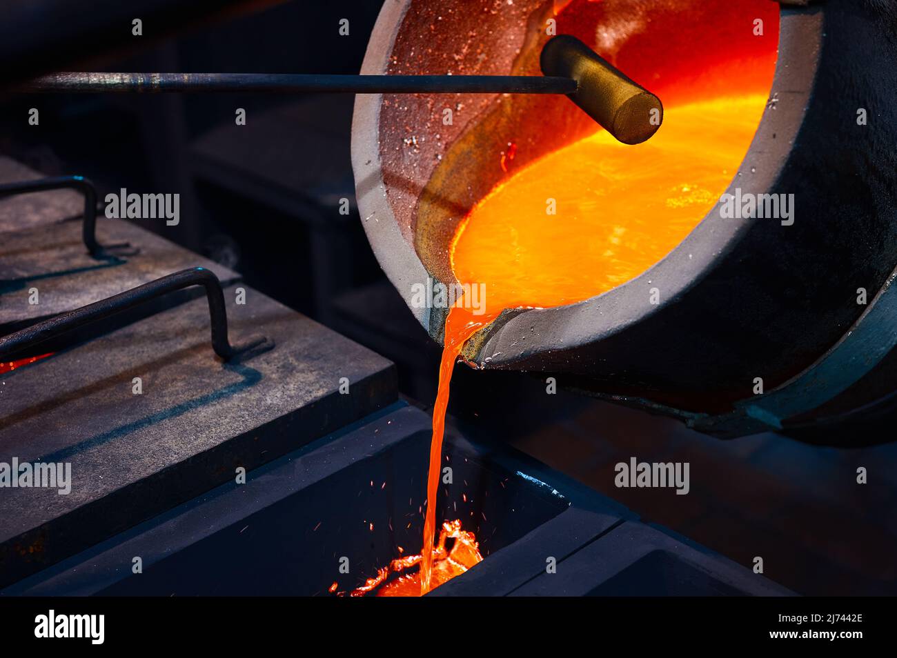 Pouring molten metal from a ladle into a rectangular graphite mold ...