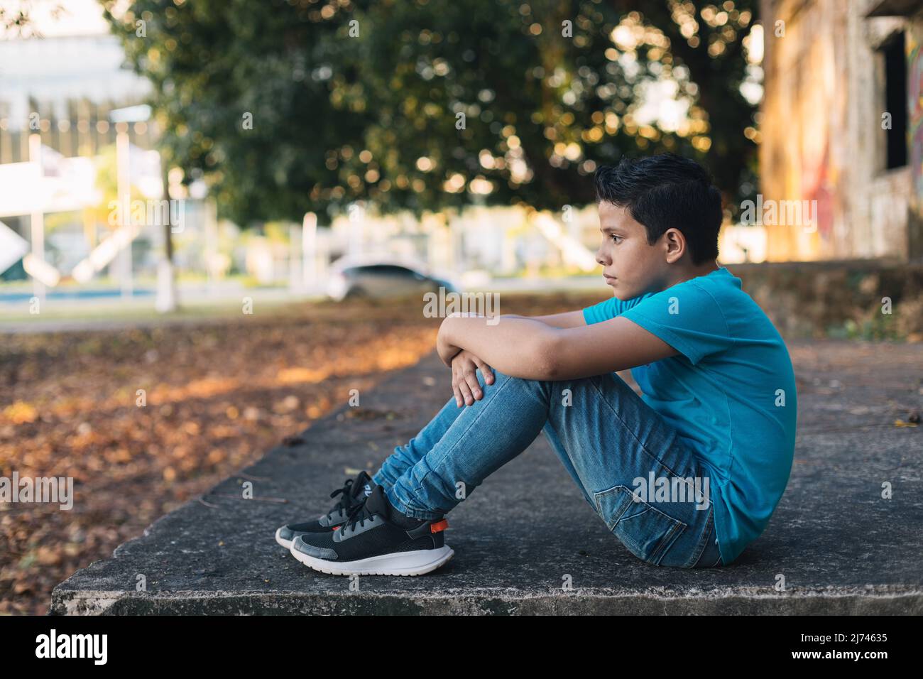 Hispanic boy sitting on some ruins looking at the horizon, with a sad ...