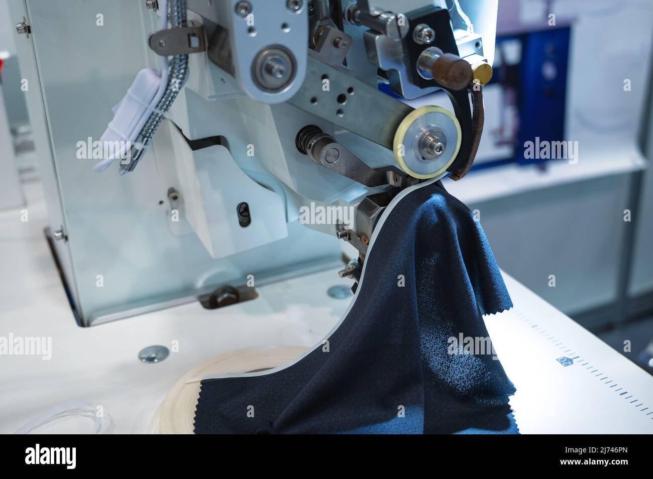 Machine sews cuff to dark blue fabric edge in workshop Stock Photo - Alamy