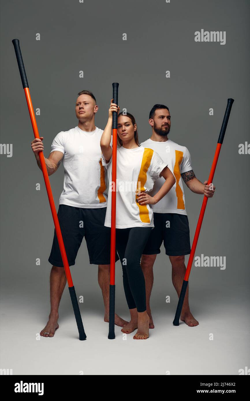 Two men and woman aikido fighters with wooden fight stick posing in ...