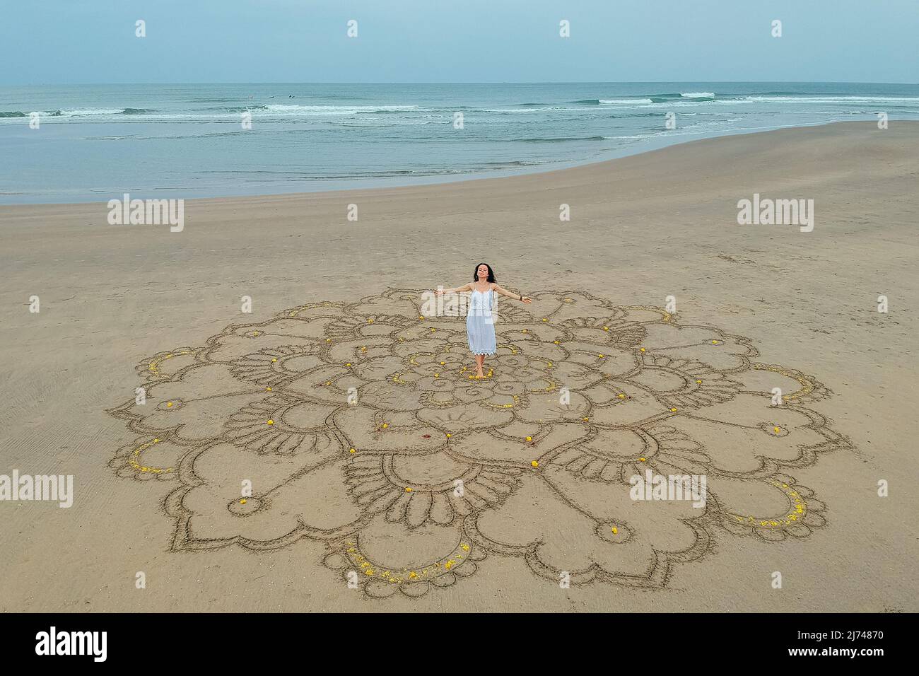 a large mandala painted on the sand on the ocean with a girl in the ...