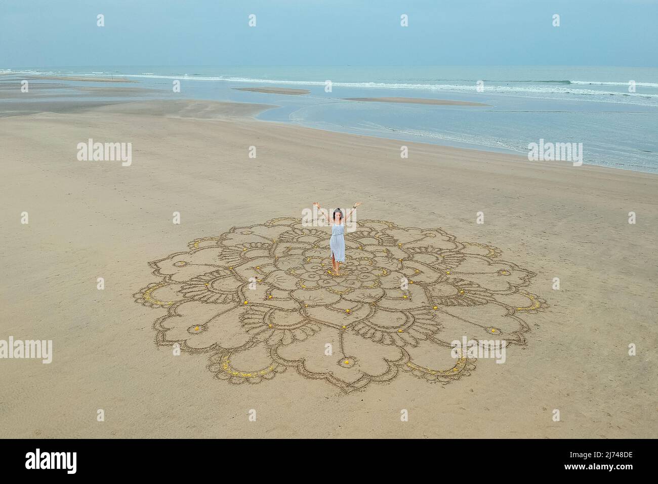 a large mandala painted on the sand on the ocean with a girl in the ...