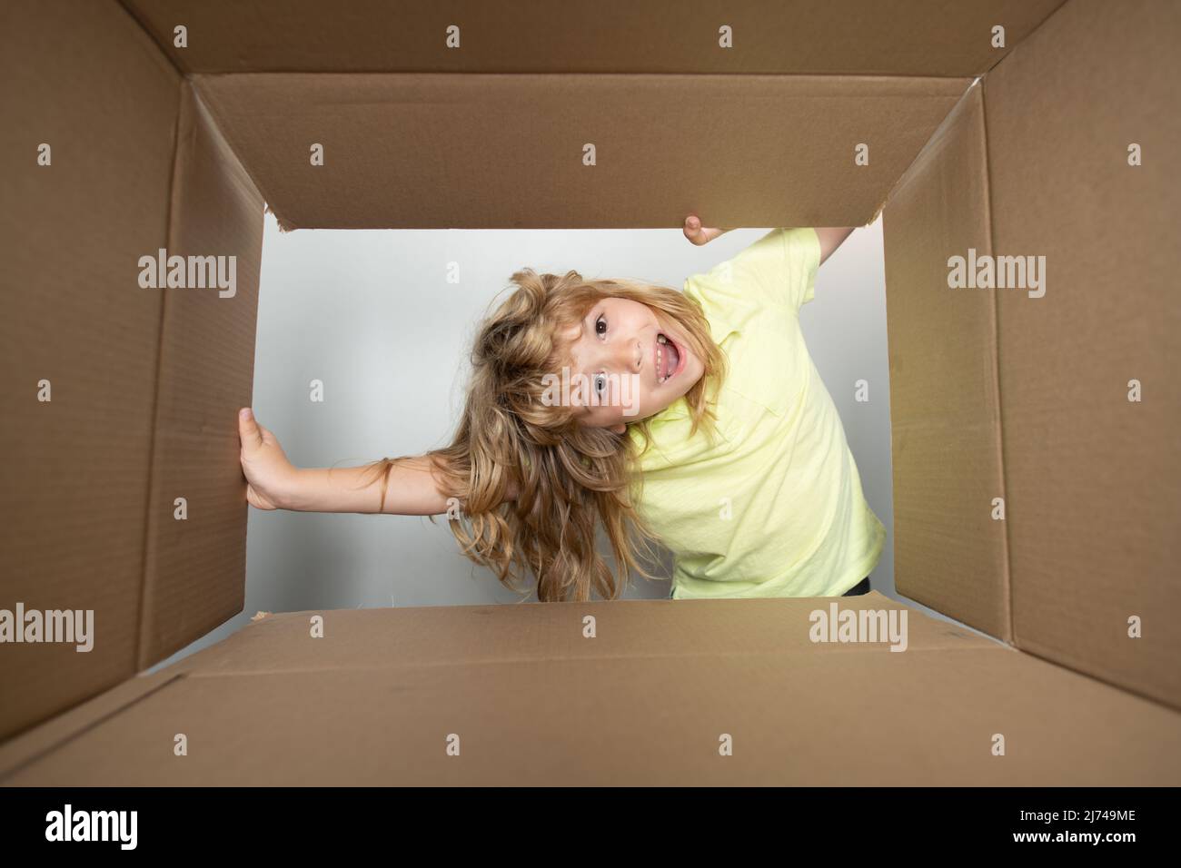 Kid unpacking and opening carton box, and looking inside with surprise ...