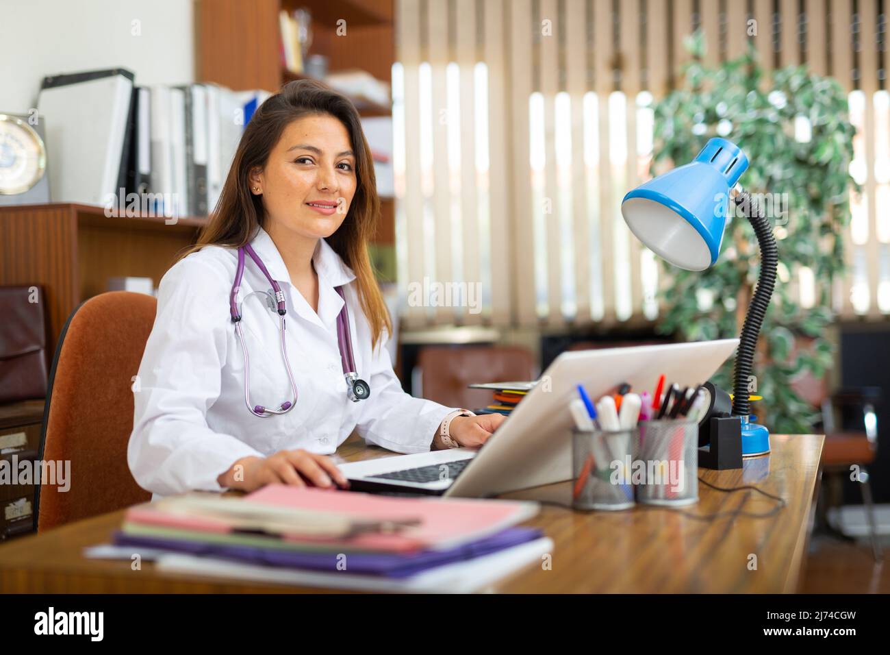 Latin american woman doctor sitting in office Stock Photo - Alamy