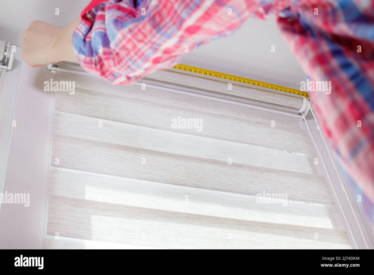 A handywoman with a tape measure installs white roller blinds indoors ...