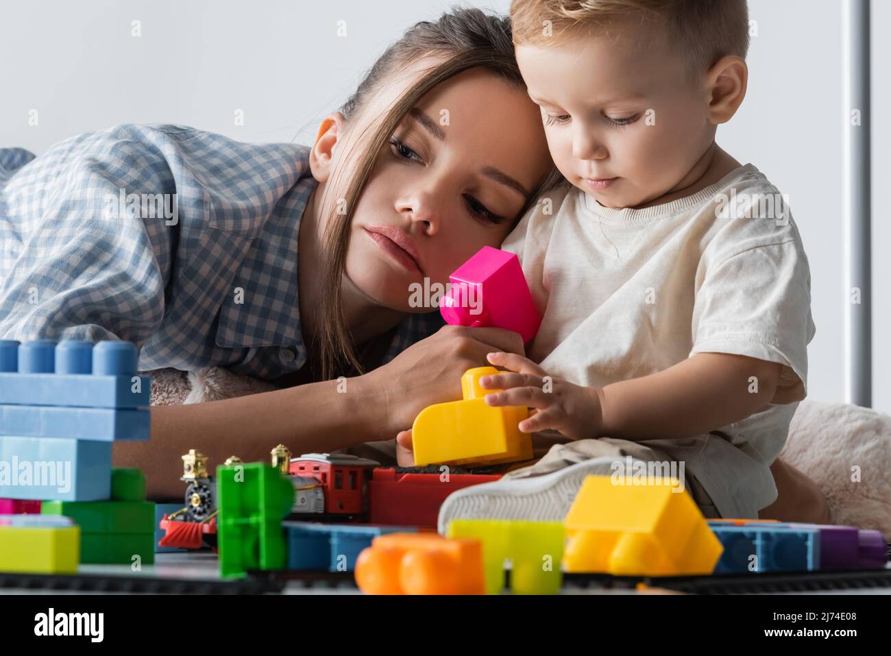 little boy playing with construction cubes near tired mom on grey Stock ...
