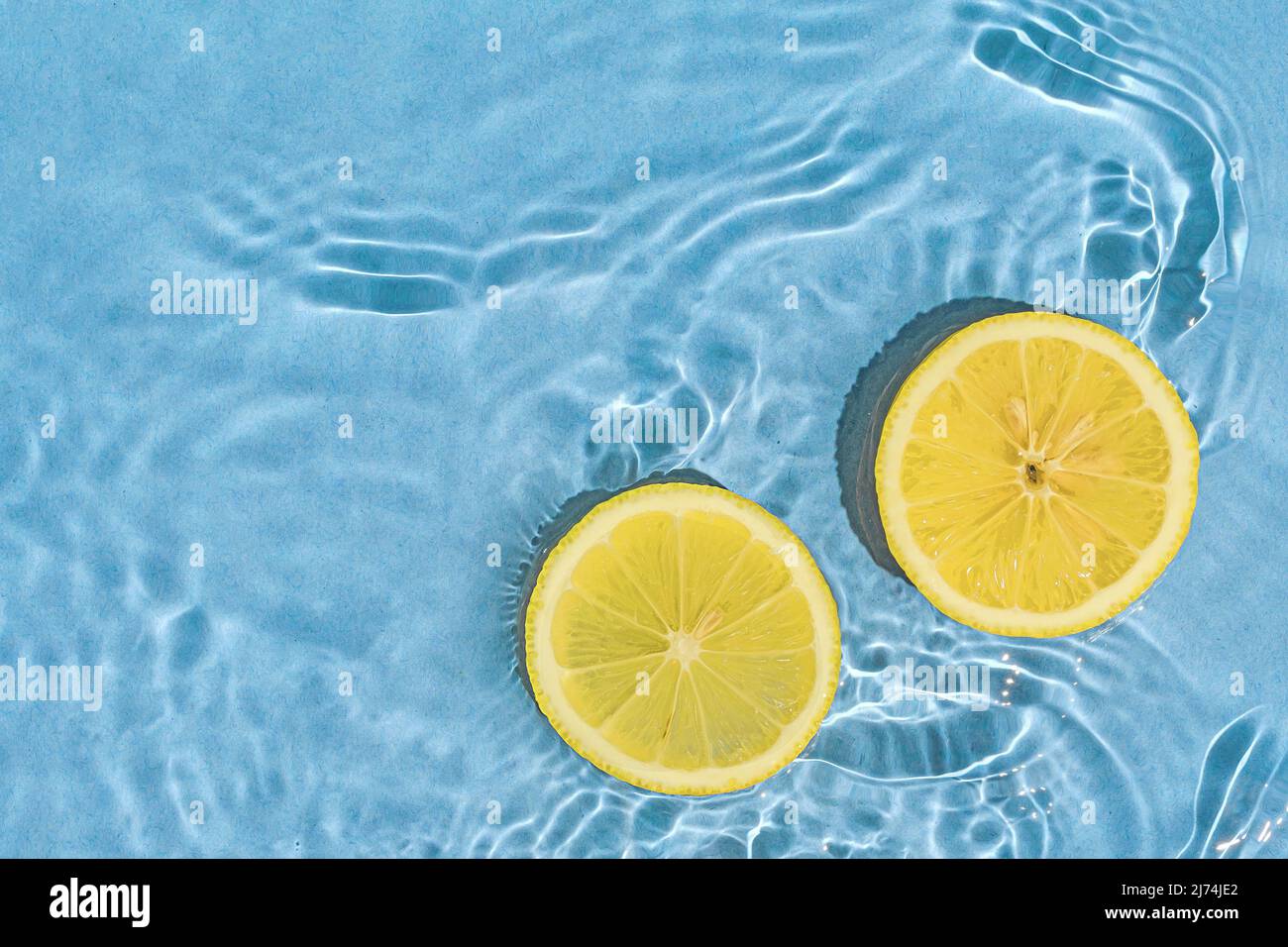 Two parts of bright yellow fresh citrus lemon fruit in blue pool with ...