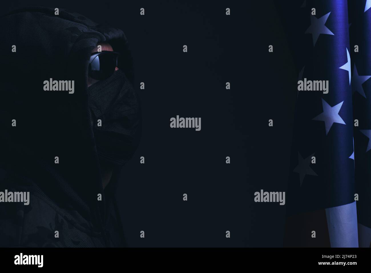 Hooded man wearing black glasses and mask looks flag of the United ...