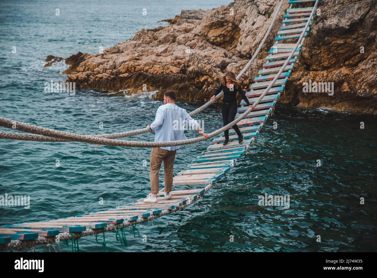 couple woman with man walking by shaky suspension bridge crossing sea ...
