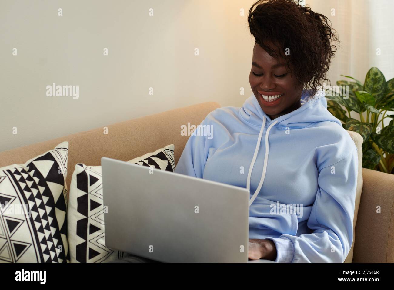 Happy excited young woman sitting on comfy sofa and coding on laptop at home Stock Photo - Alamy