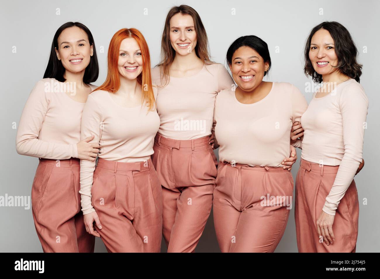 Portrait of smiling beautiful real women embracing each other against ...