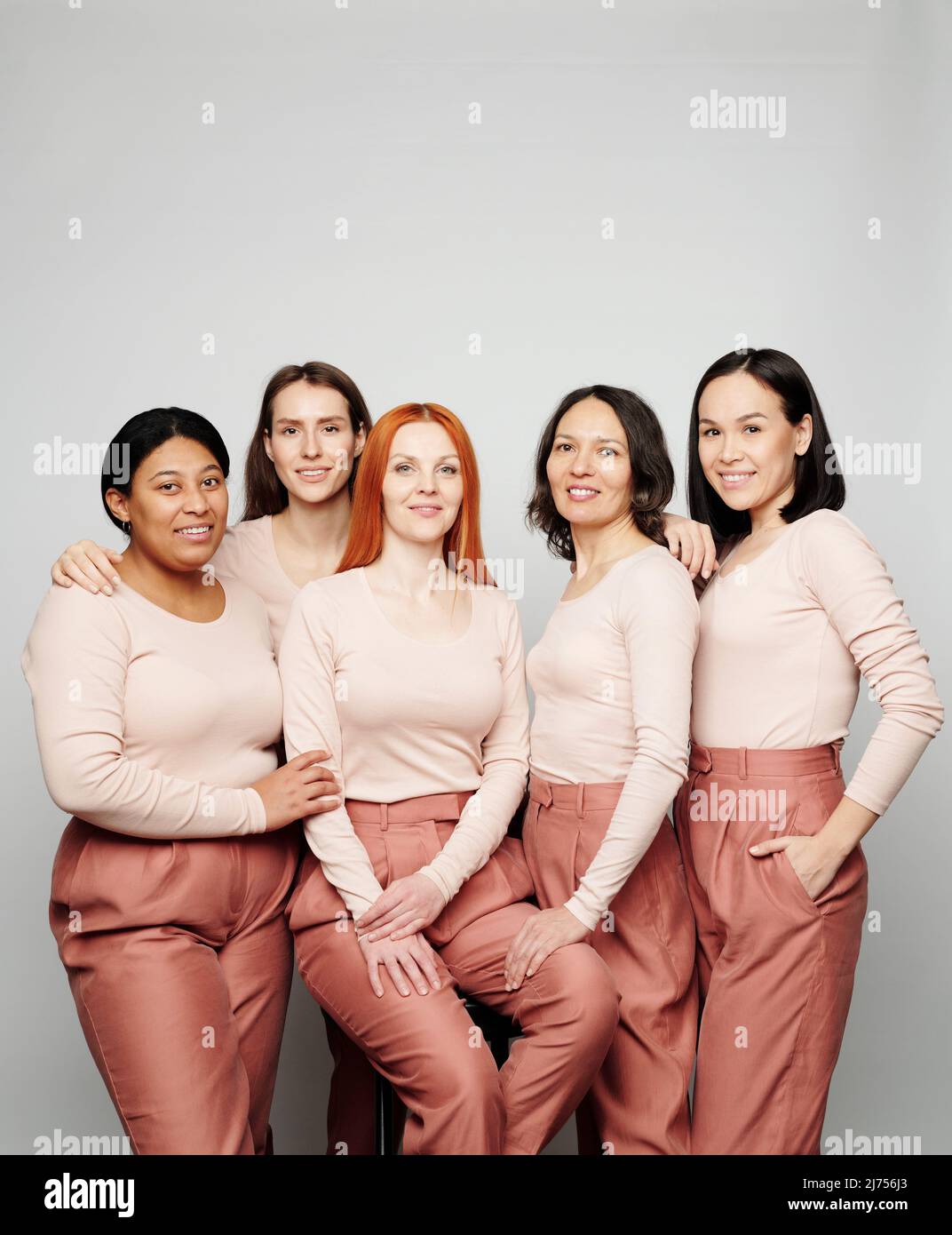 Portrait of smiling multi-ethnic women in pink outfits standing against ...