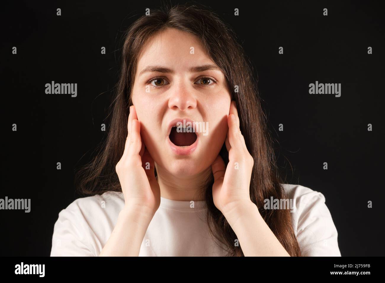 A woman with an open mouth holds her cheeks with her hands, exercises ...