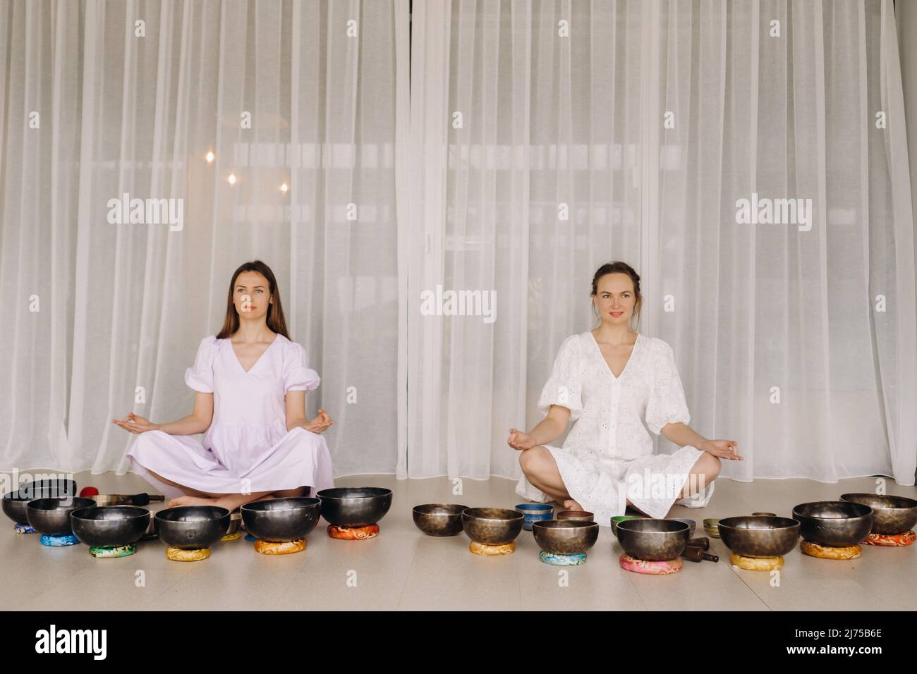 Two women are sitting with Tibetan bowls in the lotus position before a ...