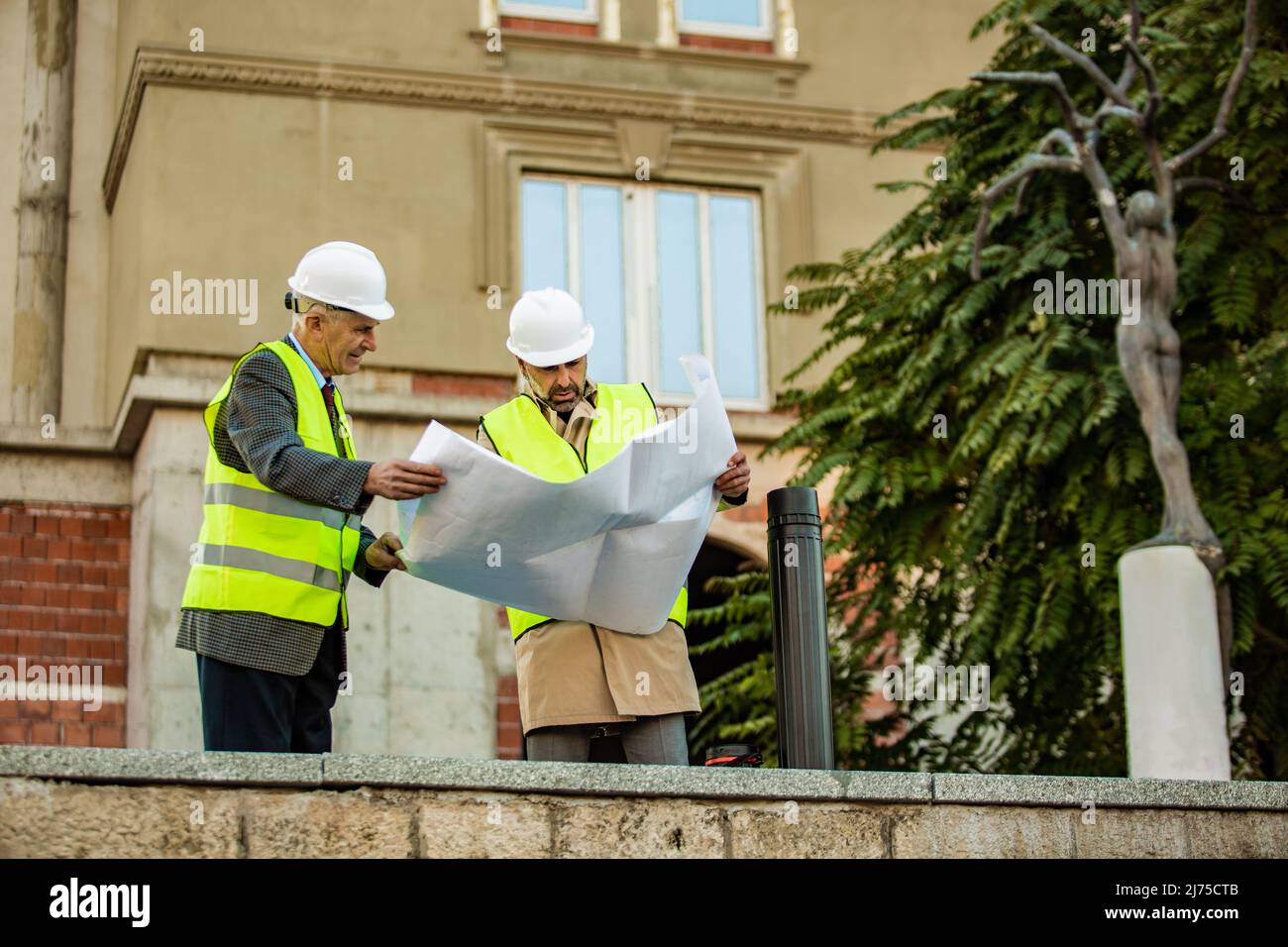 Two construction workers are looking at the plans on the paper while ...