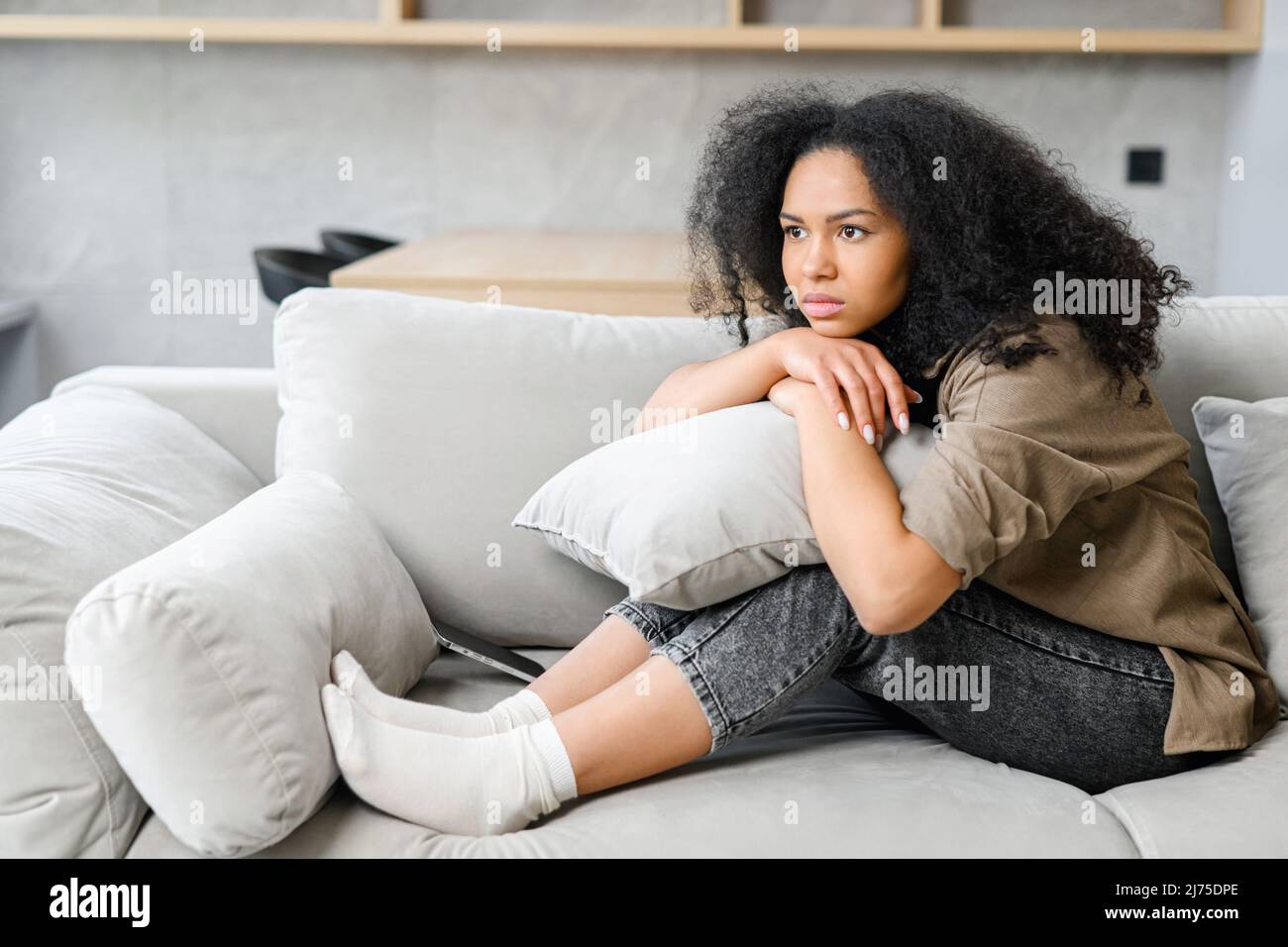 Upset depressed lady sitting on sofa, looking in the window, feeling ...