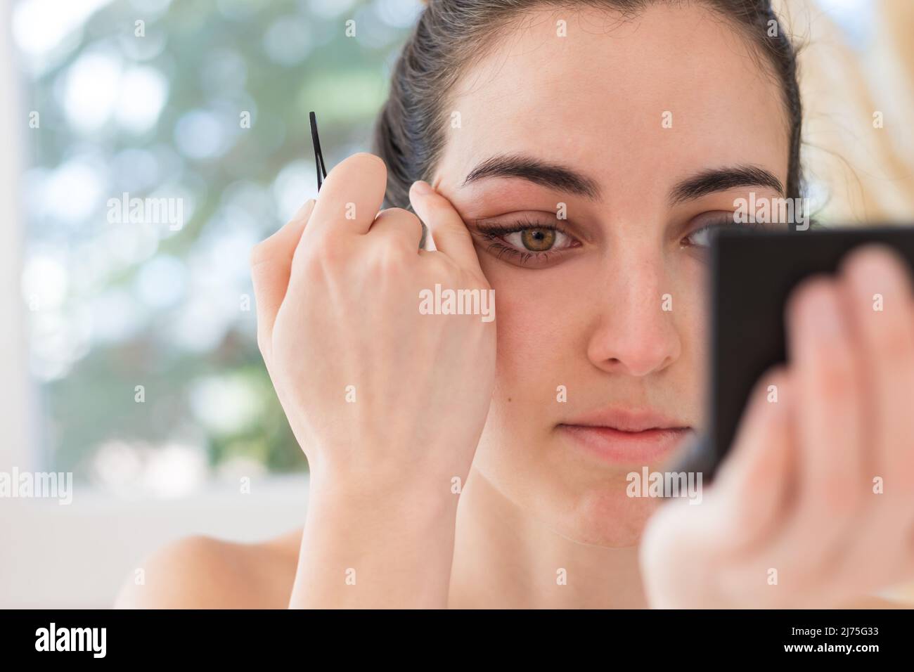 Young woman suffering from pain while tweezing her eyebrows. Wiping the ...