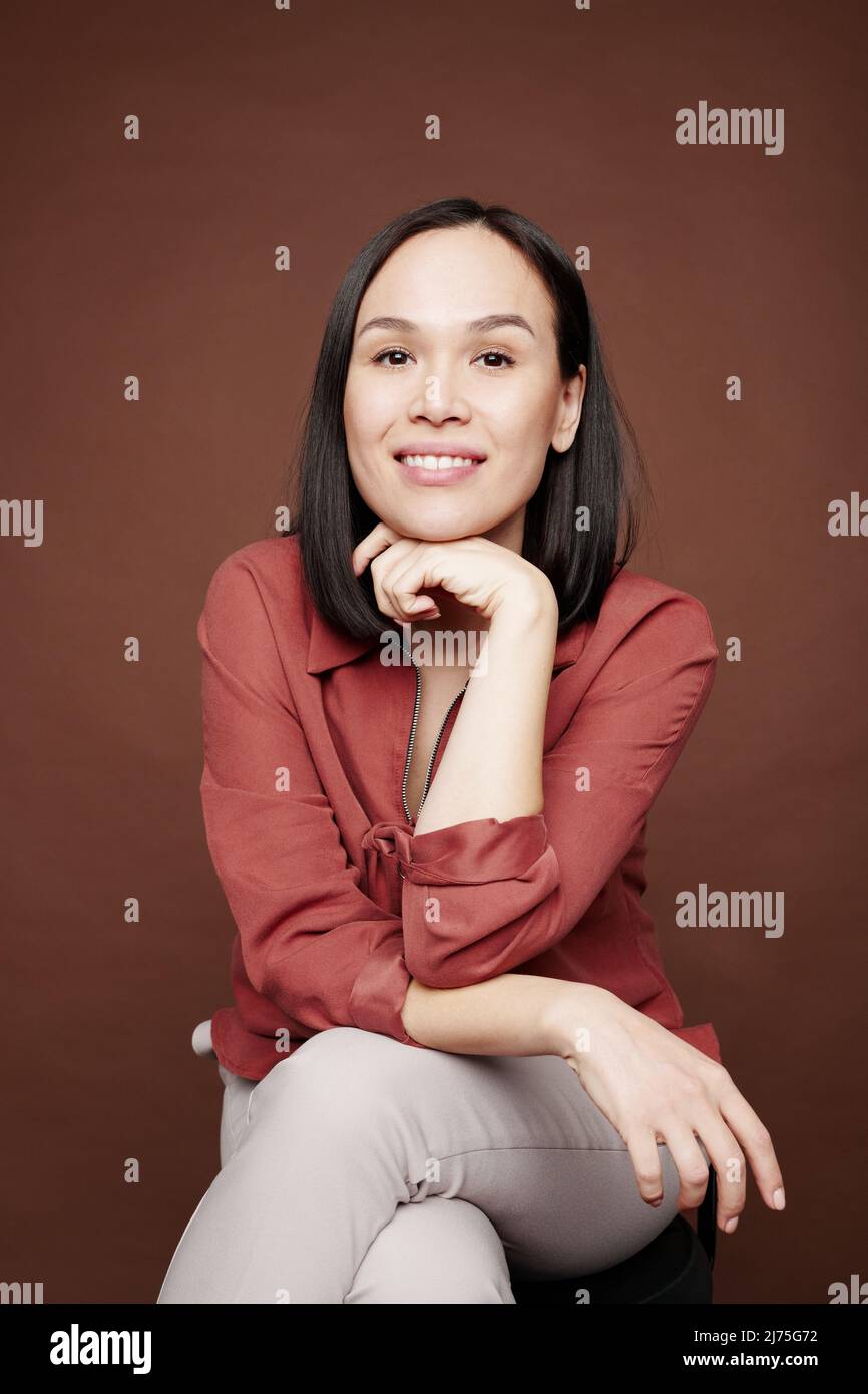 Portrait of smiling attractive Asian girl sitting on stool and leaning ...