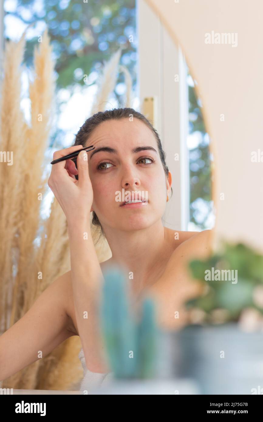Young beautiful woman pulling out eyebrows hair at home beauty sesion ...