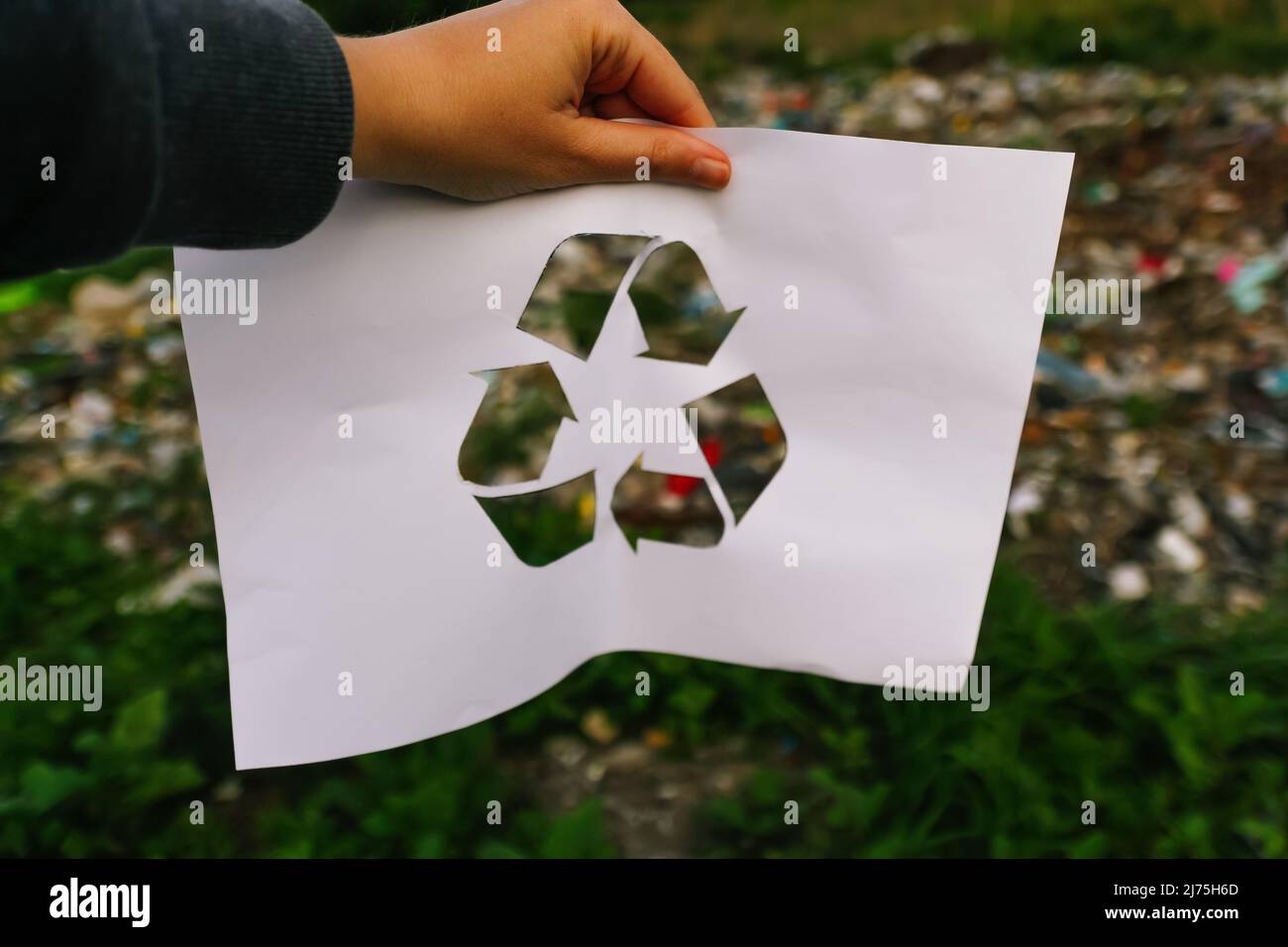 Defocus hand holding cut paper with the logo of recycling on dump ...