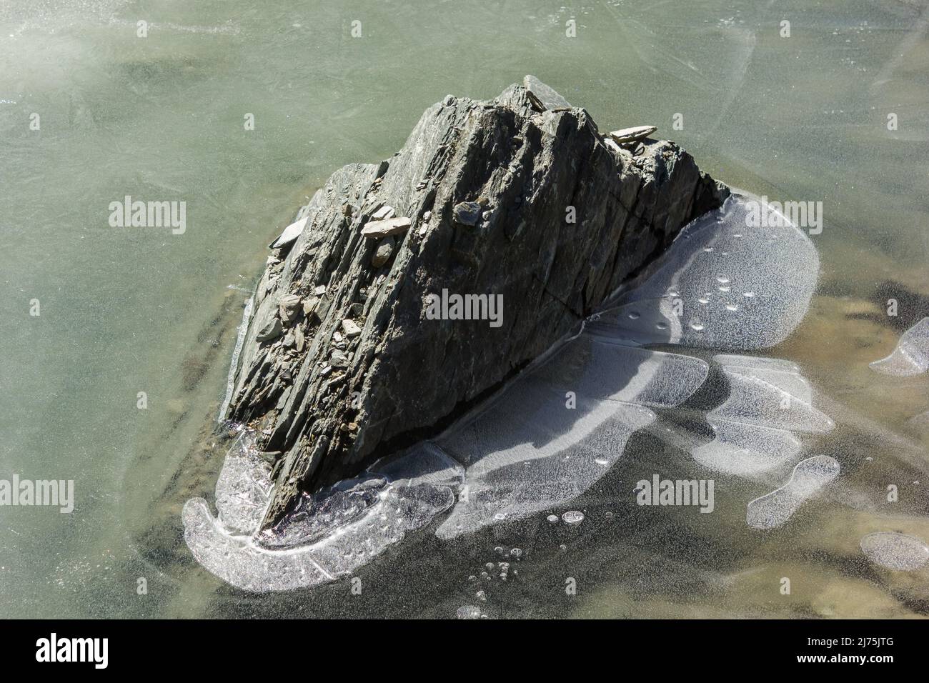 A rocky boulder surrounded by ice in the middle of a frozen lake near ...