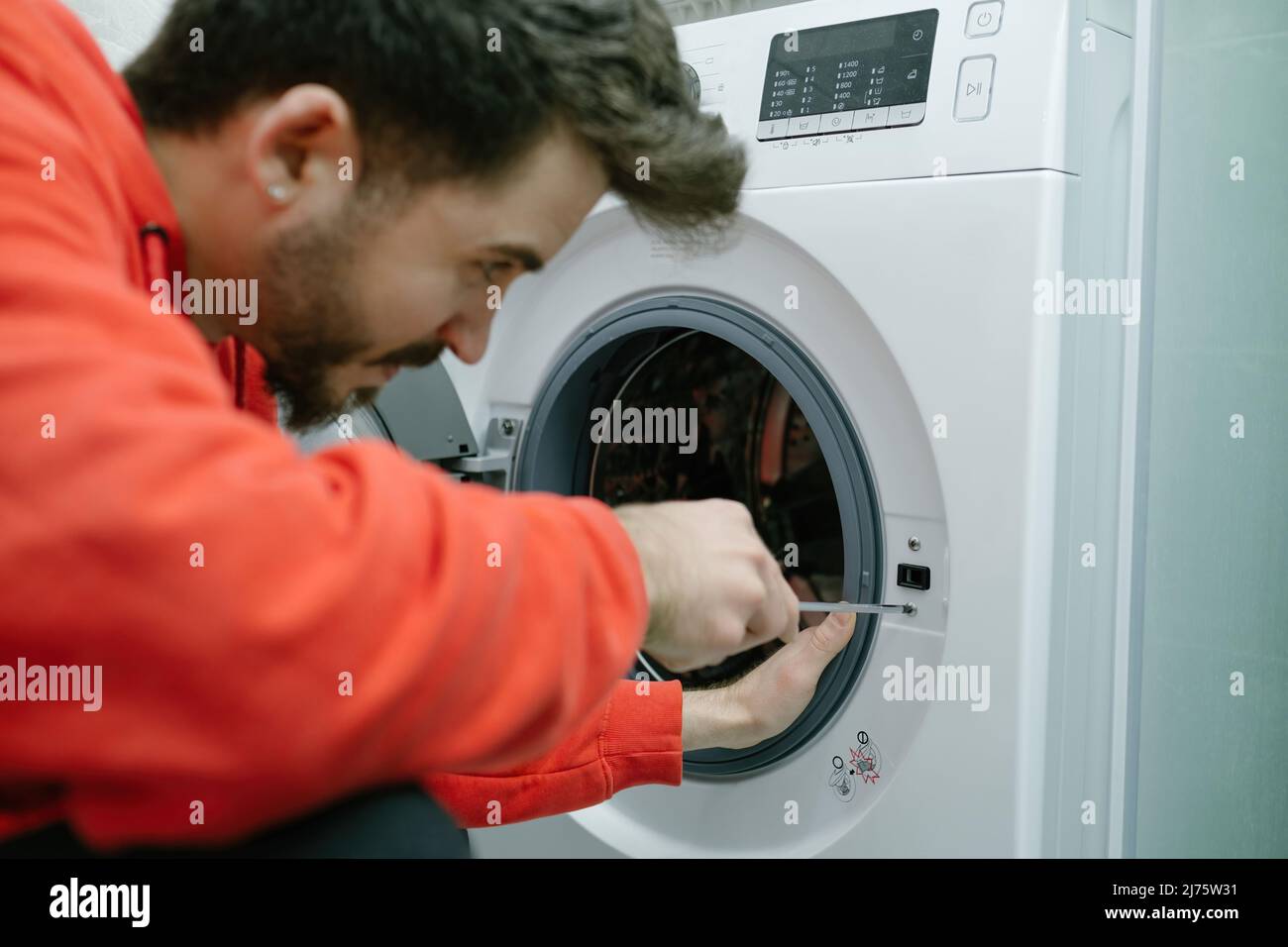 Repairman, young handsome man is repairing the broken washing machine ...