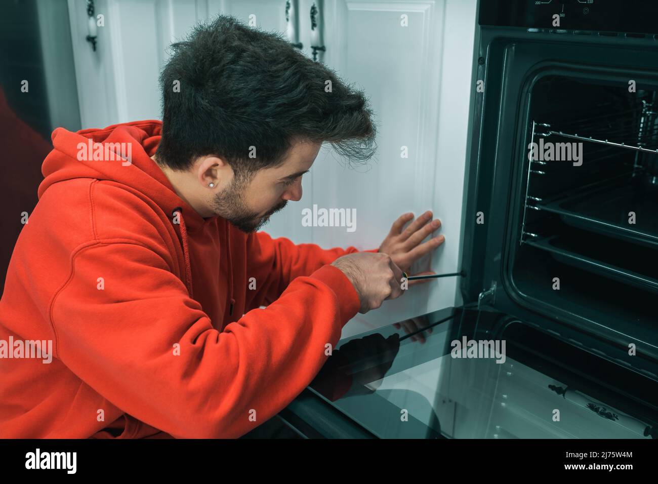 Repairman, young mechanic fixes a broken built-in oven, man using ...
