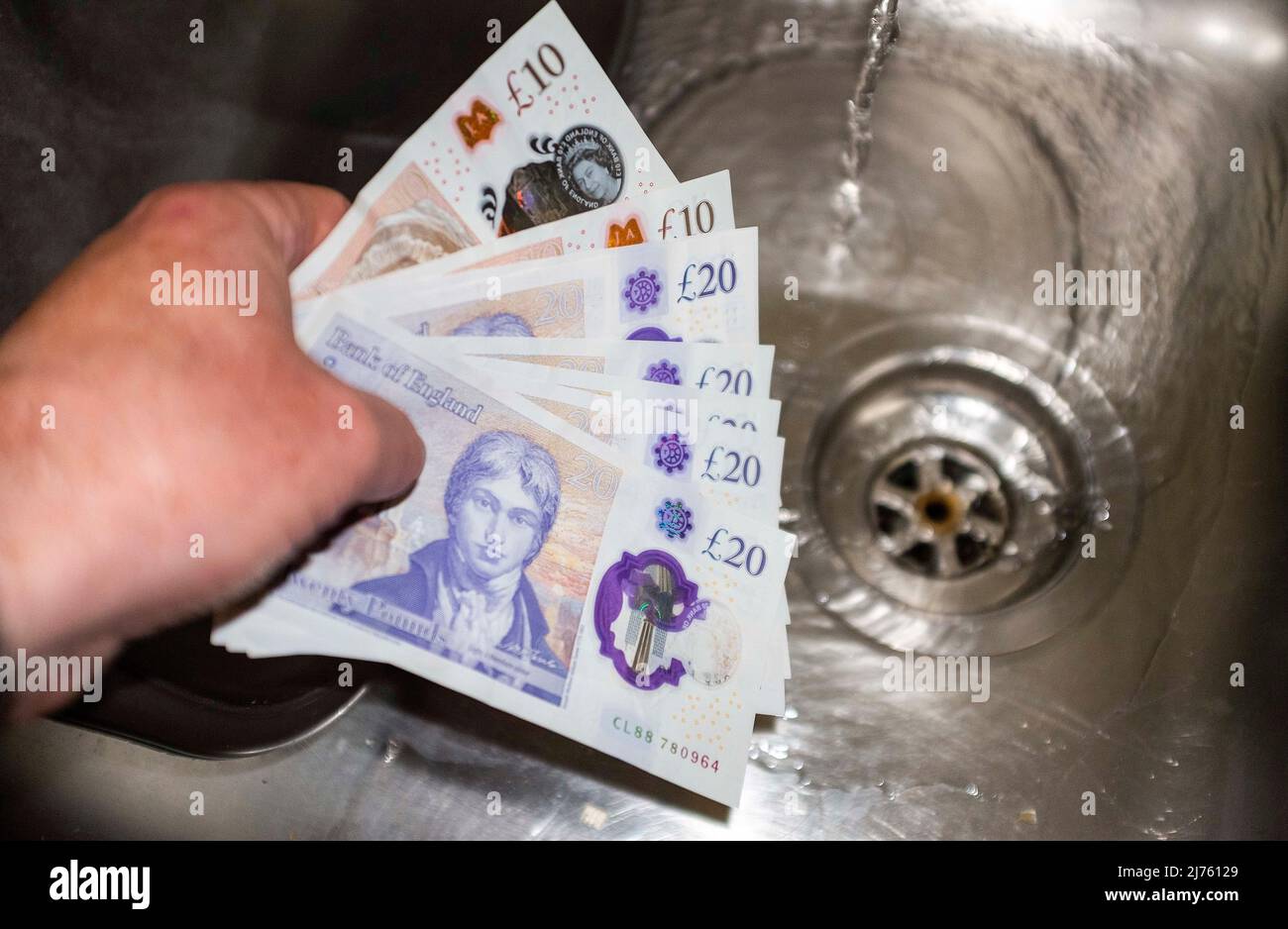 Hands holding £20 and £10 notes to illustrate cash in hand and paying ...
