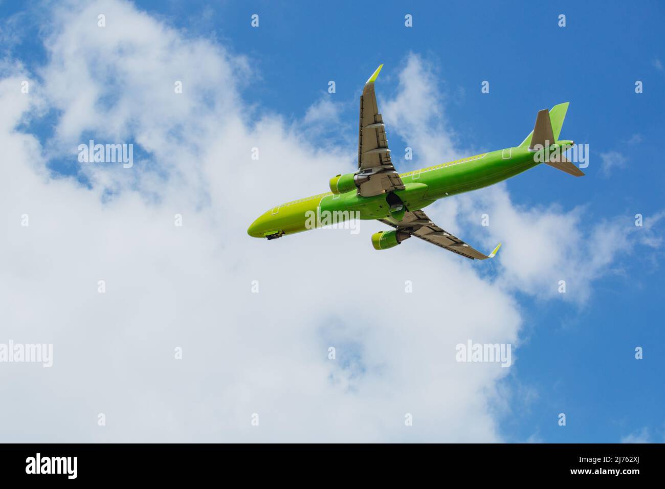 Passenger plane of yellow-green color flies in the blue sky with white ...