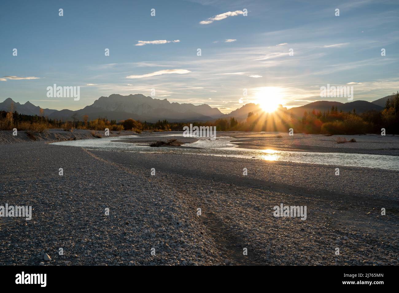 A sun star forms at sunset on the streambed of the Isar River near ...