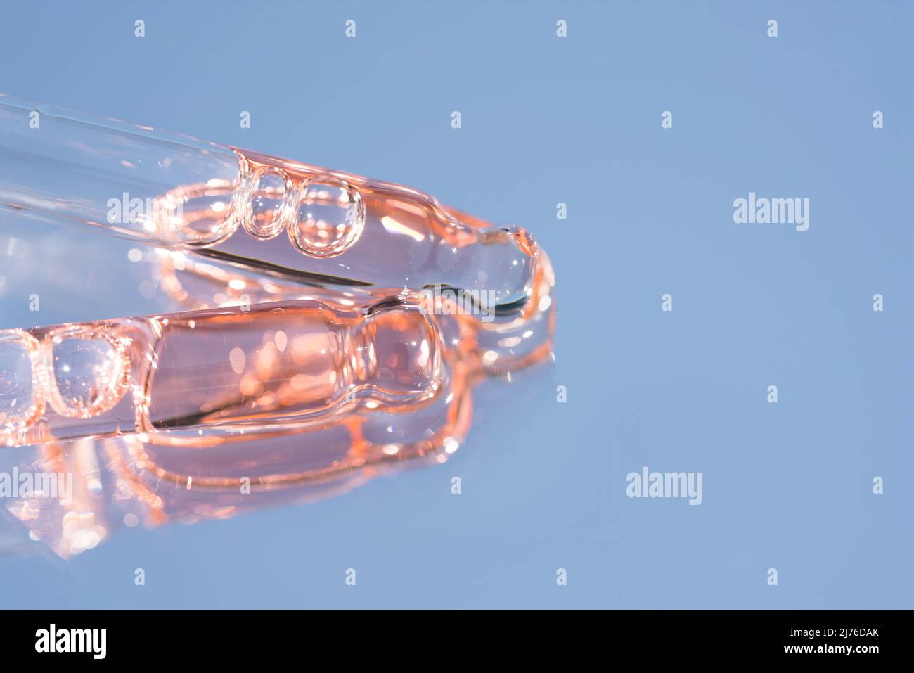 Two pipettes with pink liquid on blue glass background with copy space ...