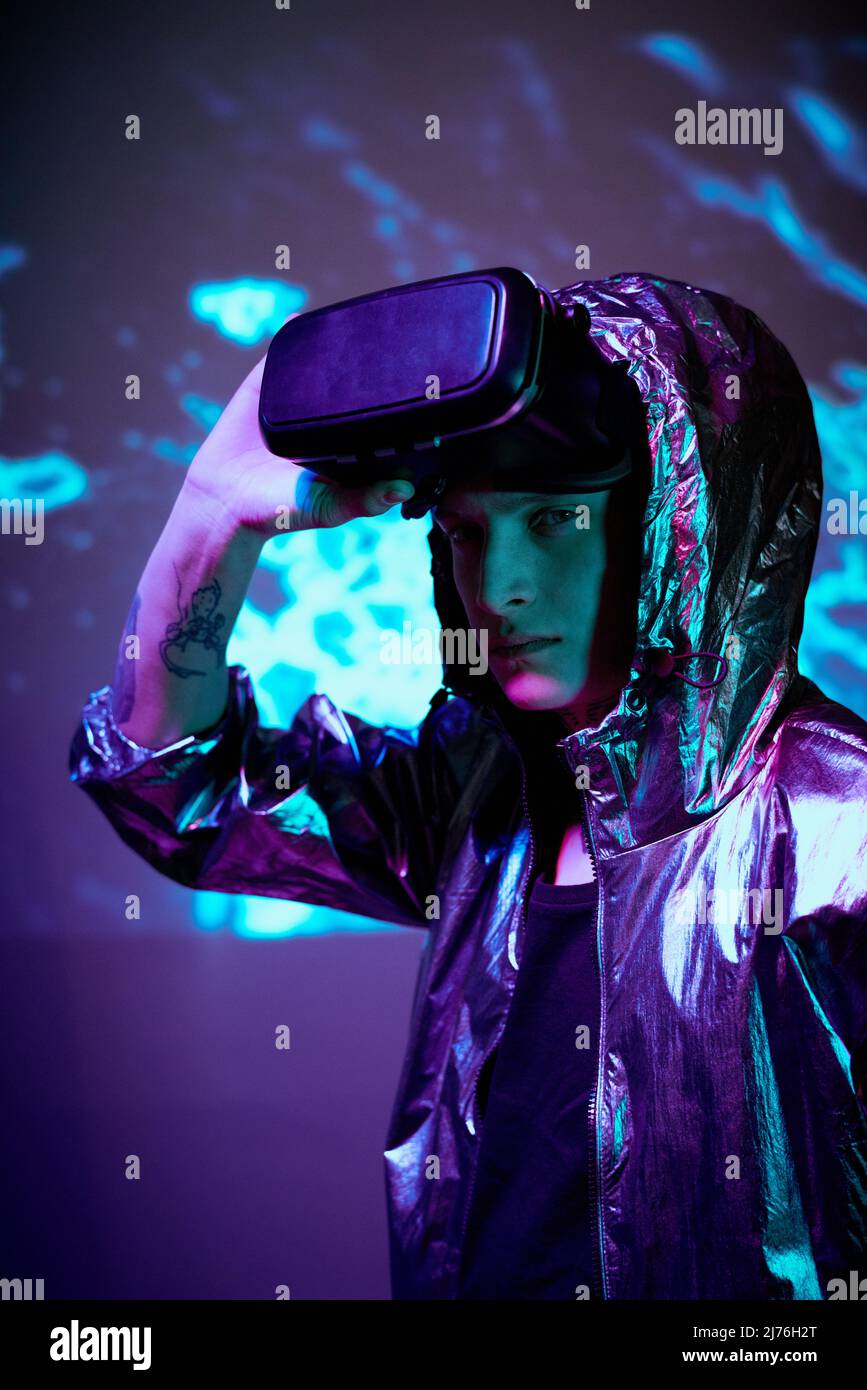 Portrait of serious young male VR gamer in hooded jacket taking off ...