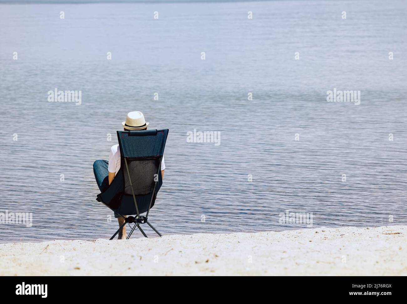 Man sitting in the folding chair on the beach, relaxing near the lake ...