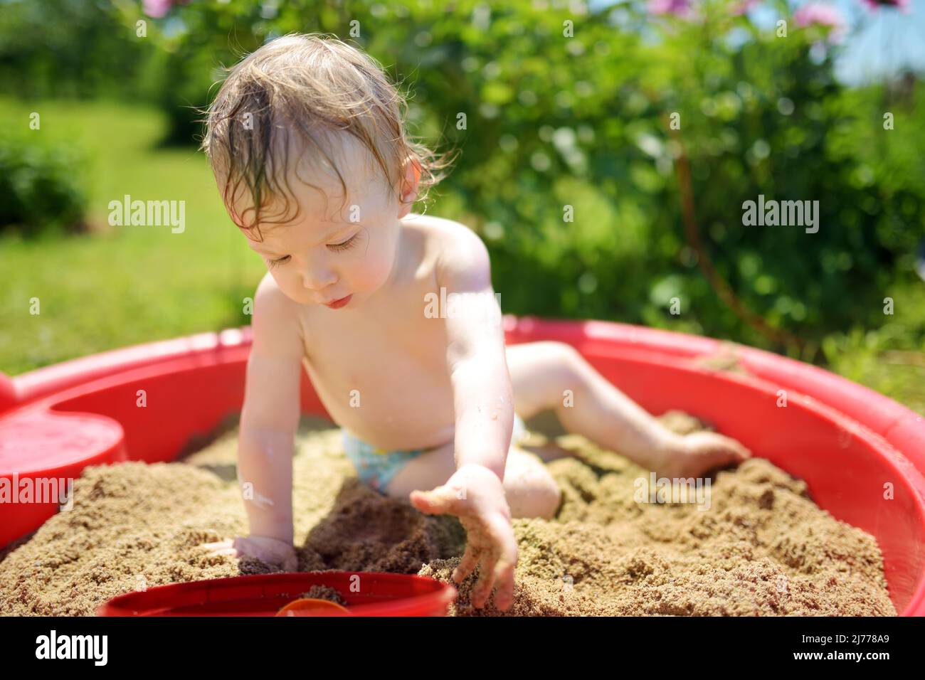Adorable toddler boy playing in a sandbox on hot and sunny summer day ...