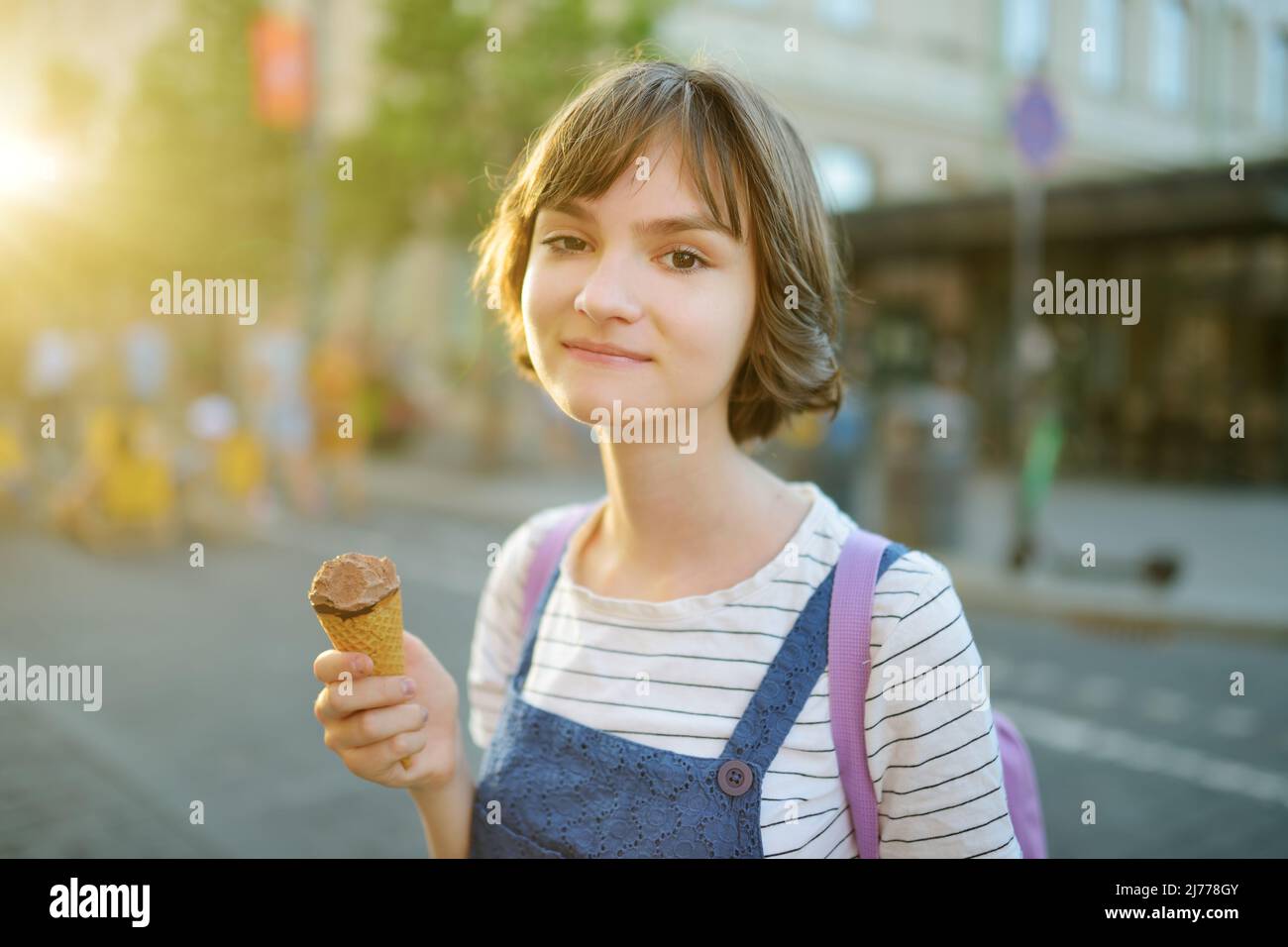 Pretty teenage girl eating tasty fresh ice cream outdoors on warm and ...