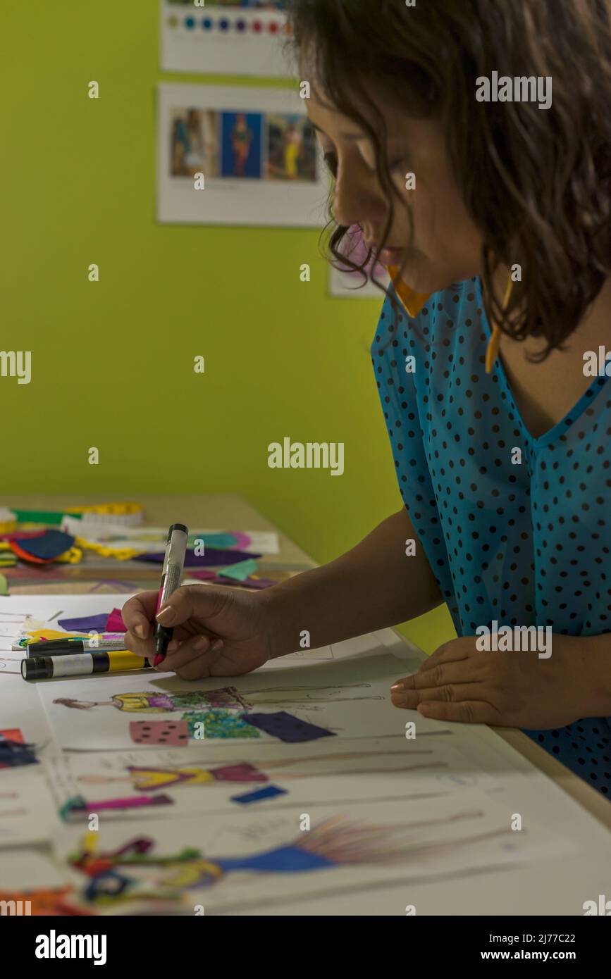 Latin fashion designer drawing dresses using markers for a collection ...