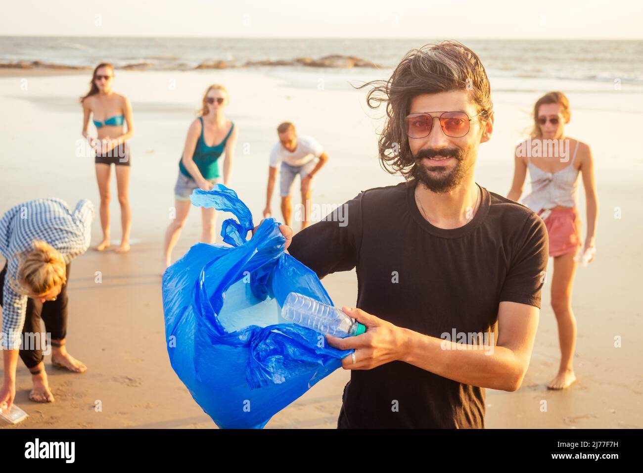 handsome indian man in the foreground collecting plastic from sand into ...