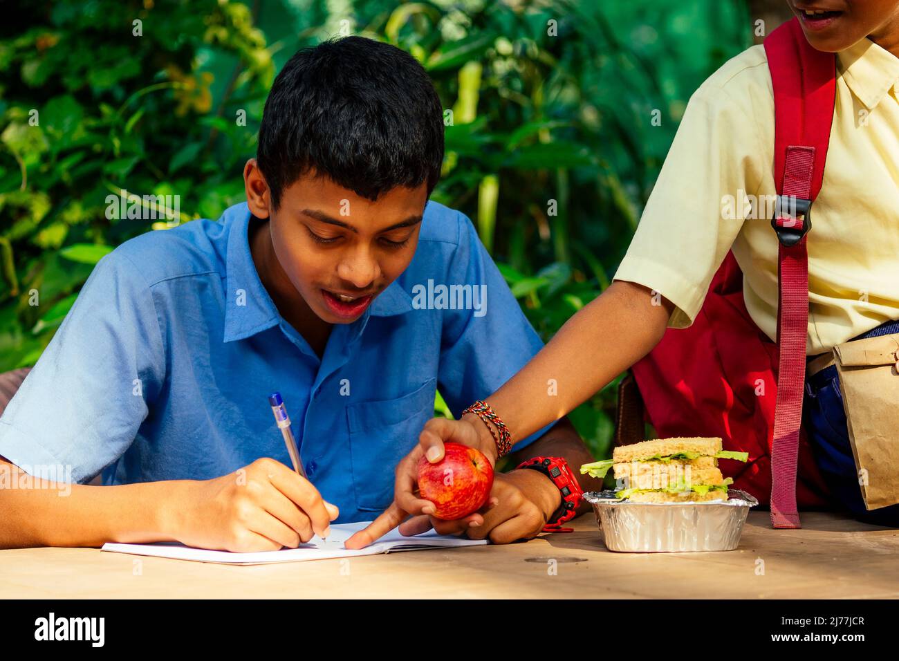 indian school boy writing on notepad doing homework , looking ...