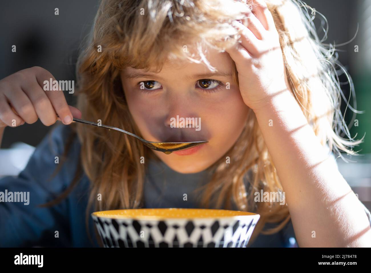 Unhappy sad child boy with spoon eats itself. Kid eating food on ...