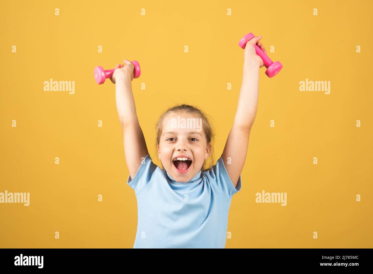 Child girl is doing exercises with dumbbells on yellow studio ...