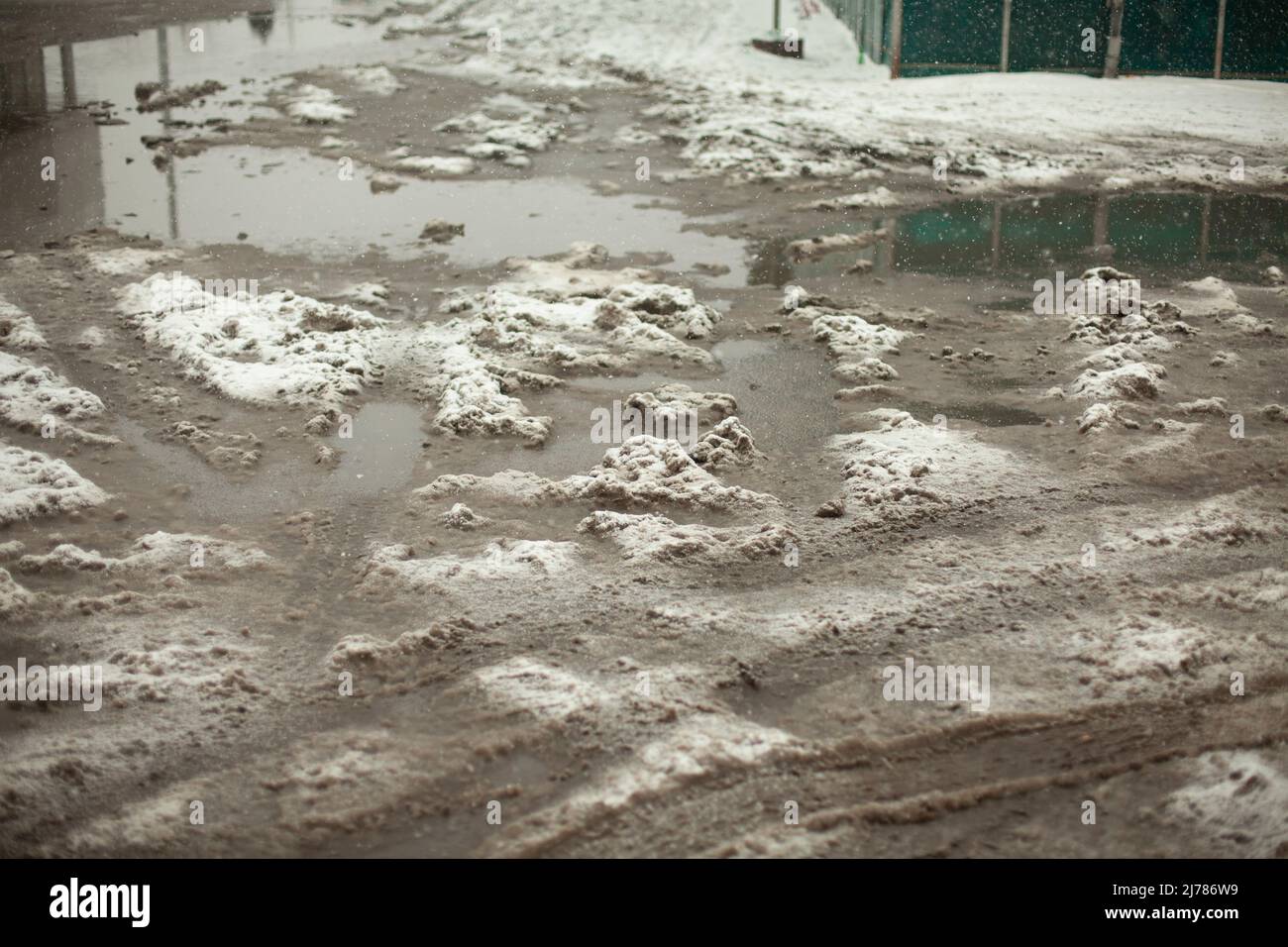 Muddy puddle of melted snow on road. Uncleaned parking. Asphalt is ...