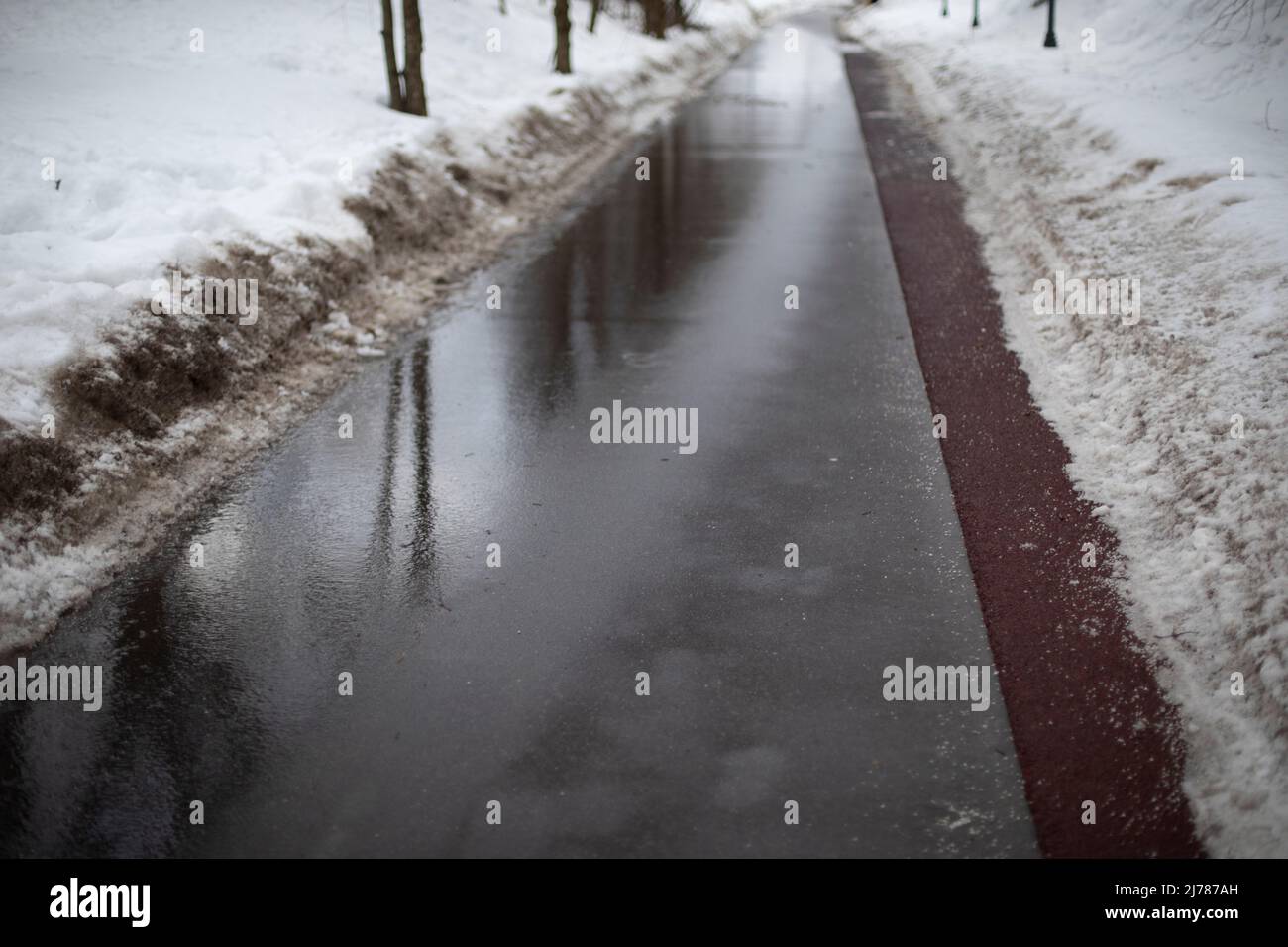 Asphalted path in park. Snow is melting on road. Details of park trail ...