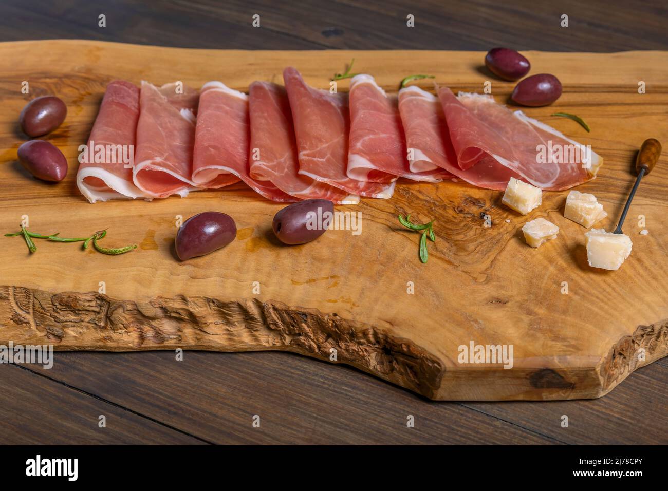 Slices of Parma ham placed on a rustic wooden cutting board with olives ...