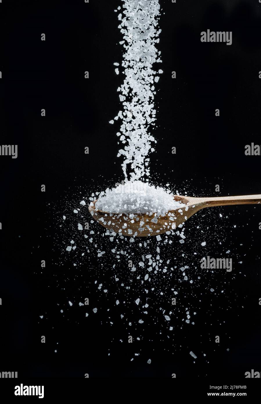 Edible salt crystals falling down into the wooden spoon at black ...