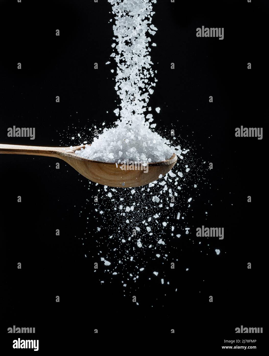 Edible salt crystals falling down into the wooden spoon at black ...