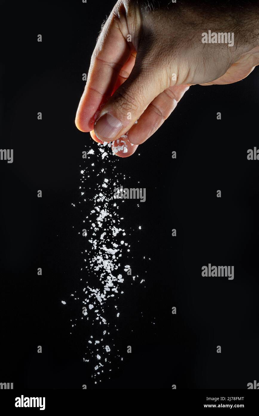 Male hand sprinkling edible salt at black background Stock Photo - Alamy